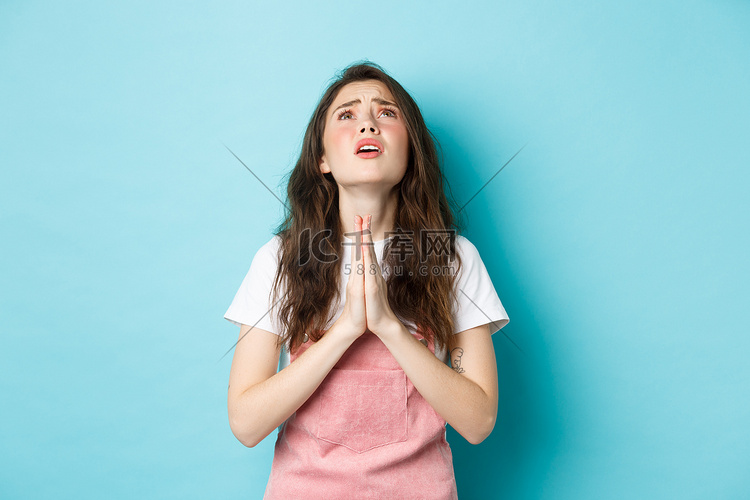 绝望的黑发年轻女子乞求上帝手牵着手祈祷满脸希望地仰望天空恳求梦想成真站在蓝色背景下高清摄影大图 千库网