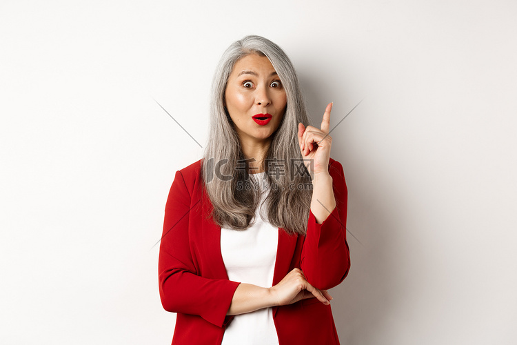 穿着红色西装外套的亚洲老年女企业家有一个想法提出一些建议以尤里卡手势举起手指站在白色背景上高清摄影大图 千库网
