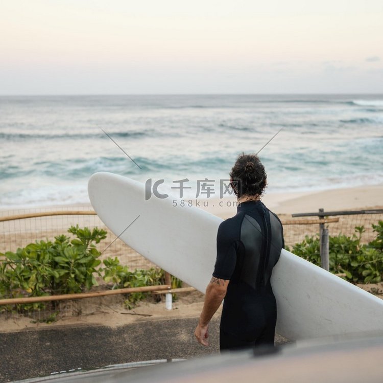 穿着冲浪服的男人拿着他的冲浪板高清摄影大图-千库网