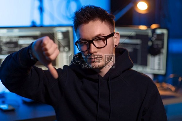 网络犯罪、黑客攻击和技术概念-年轻的亚洲黑客在黑暗的房间里戴着眼镜和连帽衫，晚上电脑显示大拇指朝下。高清摄影大图-千库网