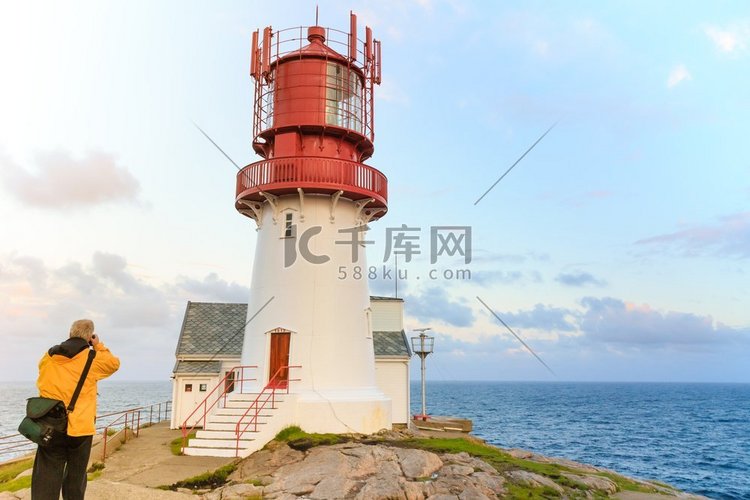 男性游客看着位于挪威南部 Lindesnes Fyr 灯塔岩石海岸边缘的历史悠久的红白灯塔。高清摄影大图-千库网