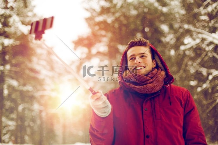 人、圣诞节、冬天和季节概念 戴着头巾和围巾的快乐微笑的男人在户外用智能手机自拍杆拍照。高清摄影大图 千库网