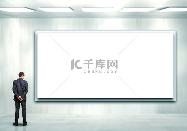 站立在一个空白的广告牌附近的商人。高清摄影大图-千库网