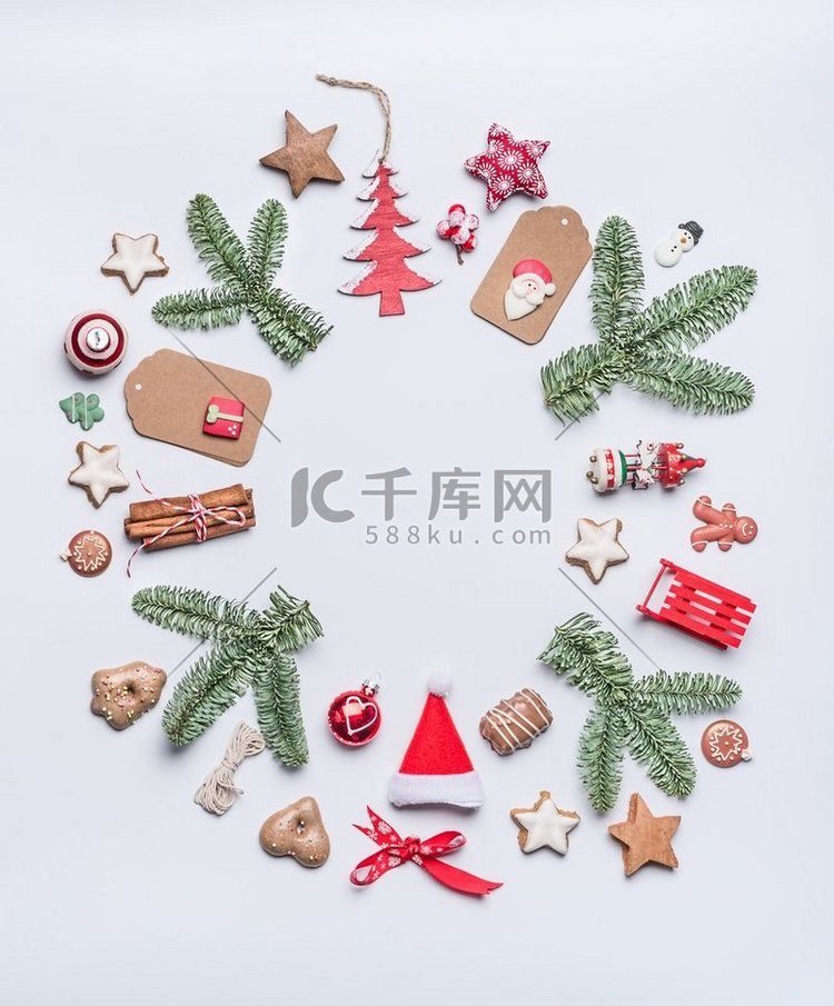 圆形圣诞框架布局组合，包括绿色冷杉早午餐、牛皮纸标签、节日饼干、巧克力、圣诞老人帽、姜饼和白色背景的红色节日装饰，顶视图。高清摄影大图-千库网