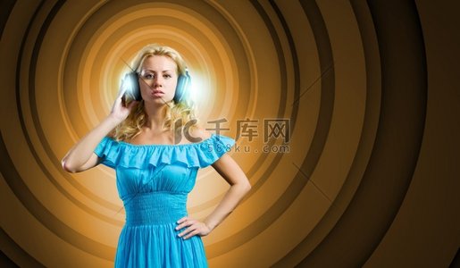 音乐爱好者。穿着蓝色连衣裙的年轻金发女孩听音乐高清摄影大图-千库网
