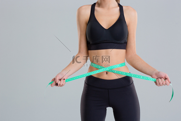 Attractive young sportswoman in tracksuit measuring the waist 高清摄影大图-千库网