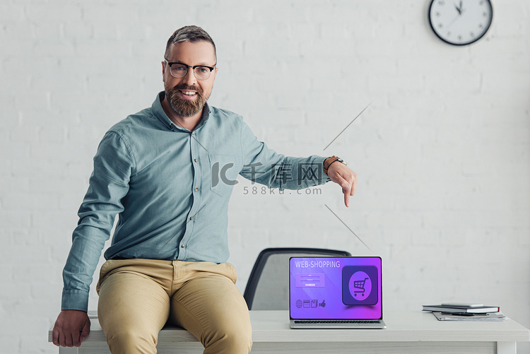 handsome businessman sitting on table and pointing with finger at ...