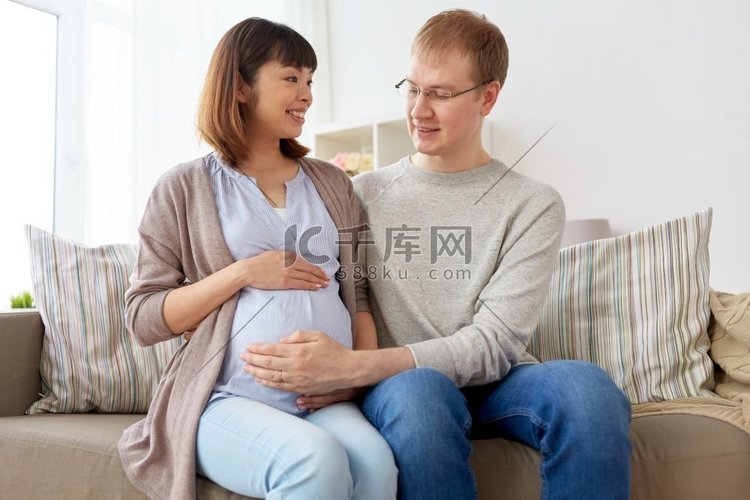 怀孕、家庭和人的概念快乐的怀孕妻子和丈夫坐在家里的沙发上。幸福的怀孕妻子，丈夫在家高清摄影大图-千库网