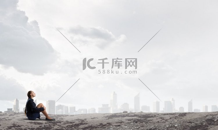 她处于绝望和孤立之中。深思熟虑的年轻女商人独自坐在岩石顶上高清摄影大图-千库网