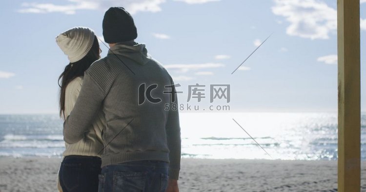 在美丽的秋日，凉爽的情侣在海滩前欢笑拥抱高清摄影大图-千库网