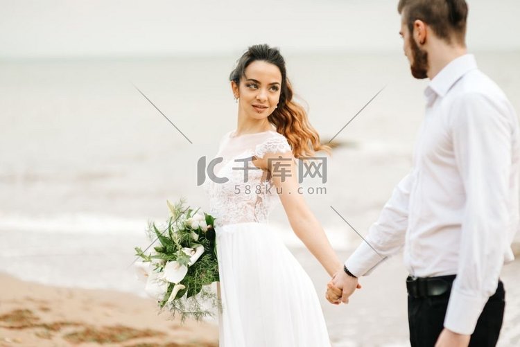 年轻的新人和新娘在沙滩上走在婚礼上高清摄影大图-千库网