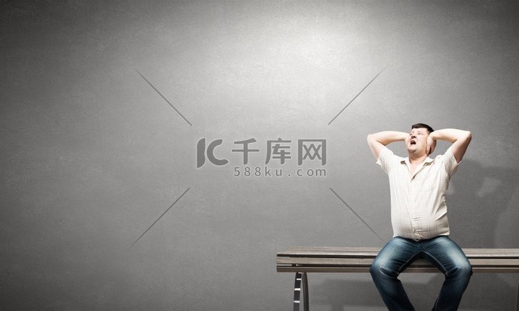坐在长凳上的胖子用手捂住耳朵。高清摄影大图-千库网