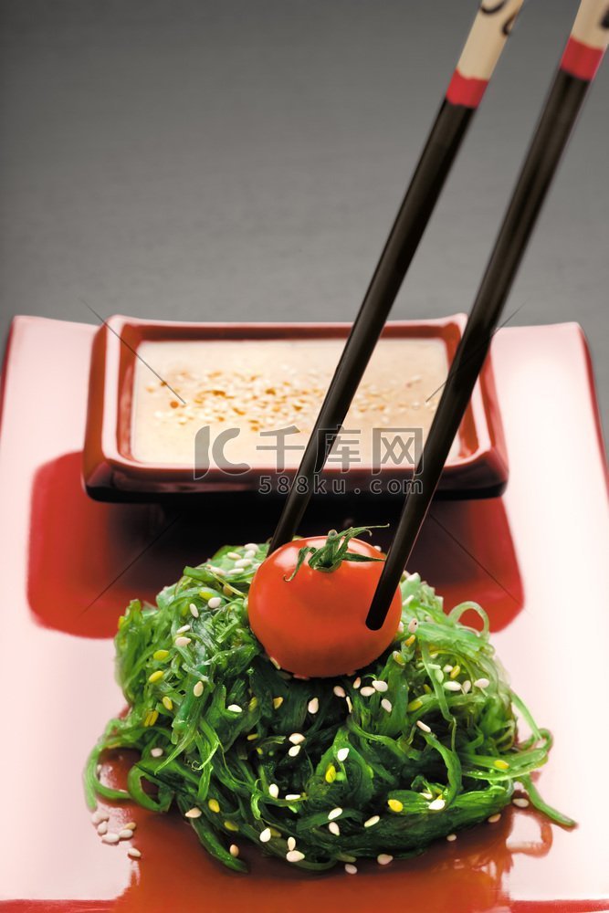 这是一张特写镜头，筷子上夹着一个红熟的西红柿，放在丘卡沙拉上，背景是果酱。高清摄影大图-千库网