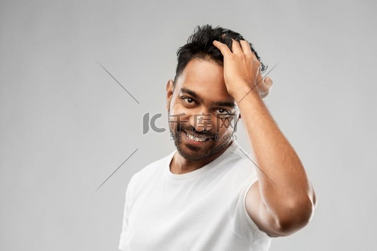 修饰和人概念—微笑的年轻印度人接触他的头发在灰色背景印度人触摸他的头发在灰色背景高清摄影大图-千库网