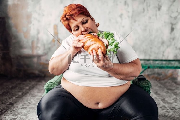 胖女人坐在椅子上吃三明治，暴食症和超重。不健康的生活方式，肥胖。胖女人坐在椅子上吃三明治，暴食症高清摄影大图-千库网