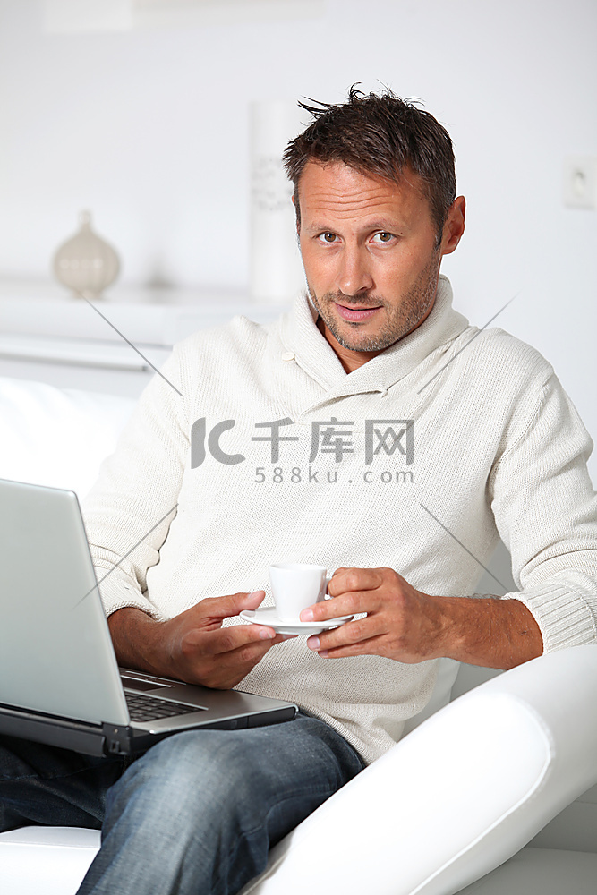 坐在沙发上拿着笔记本电脑的男人高清摄影大图-千库网