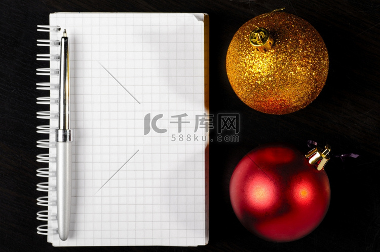 装饰圣诞球与记事本在黑暗的桌子上高清摄影大图-千库网