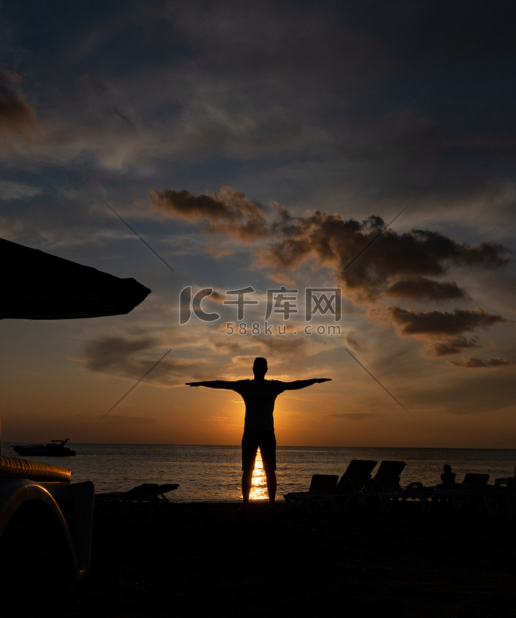 一个男人张开双臂站在夕阳下的剪影。高清摄影大图-千库网