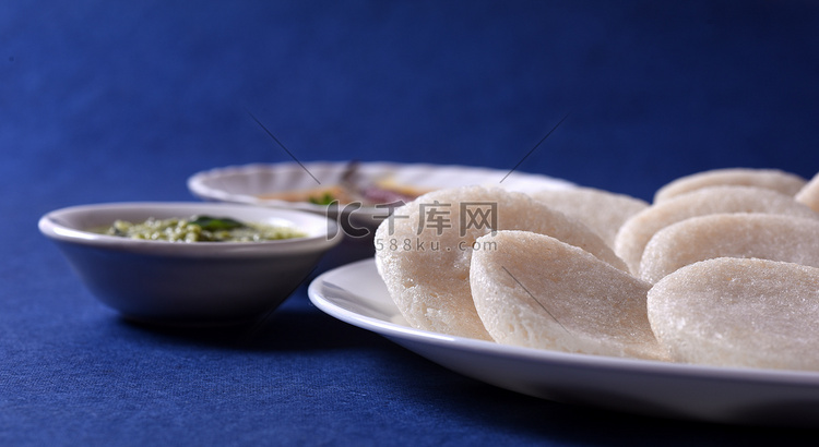 Idli 与 Sambar 和椰子酸辣酱在蓝色背景，印度菜：南印度最喜欢的食物 rava idli 或 semolina idly 或 ...