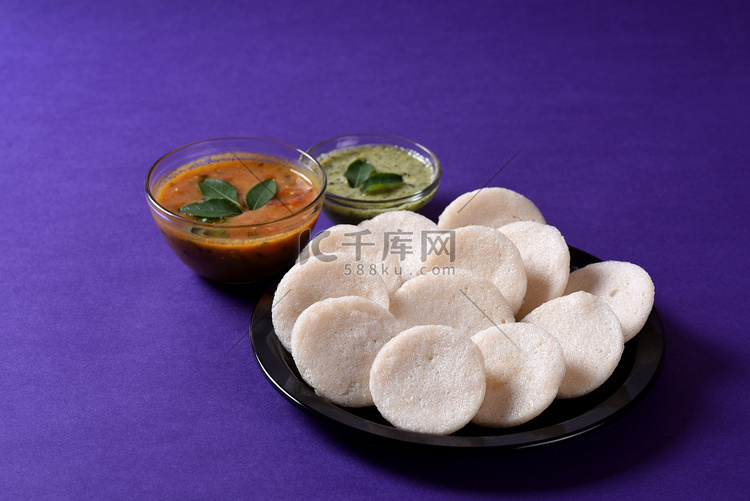 Idli 与 Sambar 和椰子酸辣酱在紫罗兰背景，印度菜：南印度最喜欢的食物 rava idli 或 semolina idly 或 ...