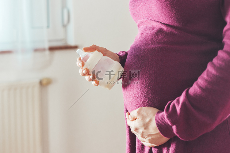 快乐的妈妈抱着她怀孕的肚子，拿着奶瓶高清摄影大图-千库网