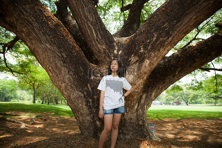 年轻女子站在一棵大树下。高清摄影大图-千库网