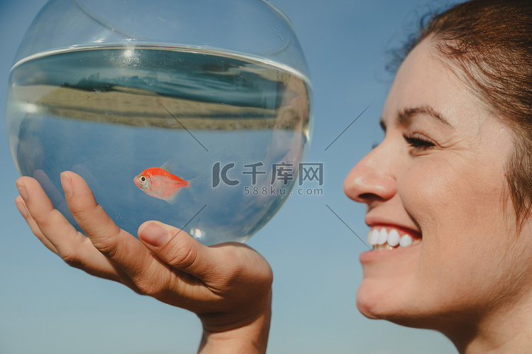 女人拿着圆形水族馆与蓝天背景上的金鱼。高清摄影大图-千库网