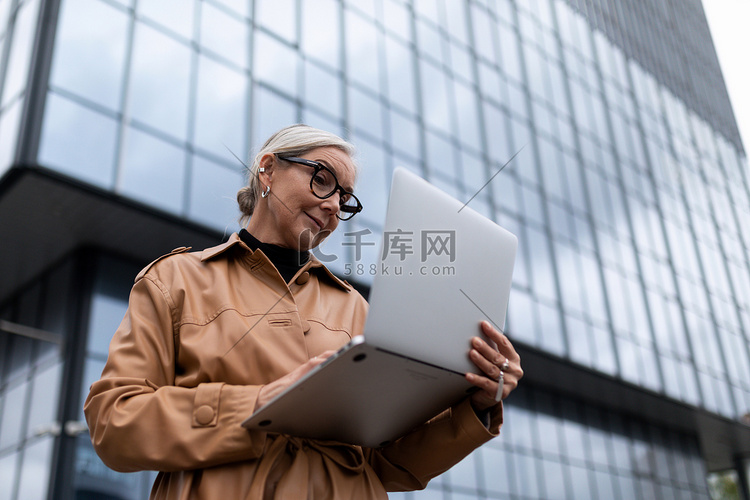 建筑背景中带笔记本电脑的成功成熟成年女性老板的水平照片高清摄影大图-千库网