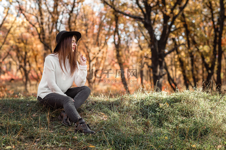 美丽的女人在阳光明媚的秋日坐在草地上。高清摄影大图-千库网