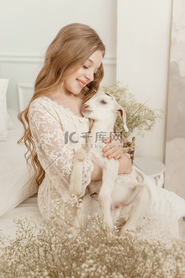 一个长头发的金发女孩坐在沙发上，家里有一只山羊。高清摄影大图-千库网