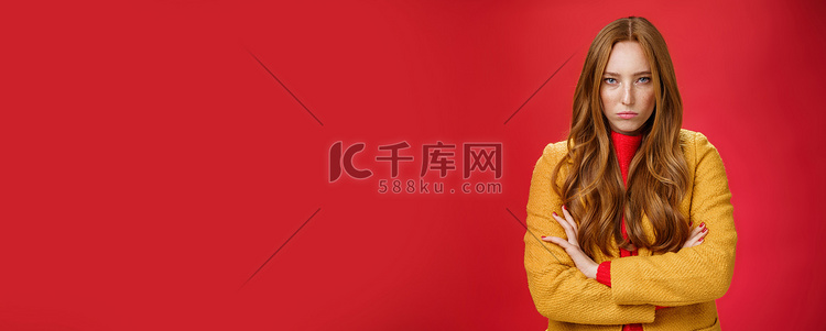 被冒犯和愤怒的红发女友表示沮丧和仇恨,因为等待时间太长,双手交叉在胸前,摆出防御和攻击性的姿势,噘着嘴,蔑视红色背景高清摄影大图 千库网