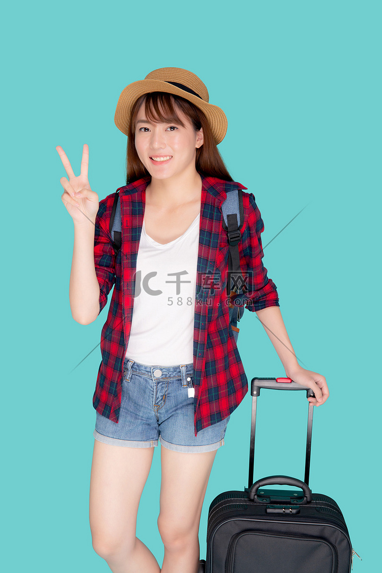 美丽的年轻亚洲女人拉着蓝色背景中突显的手提箱,亚洲女孩兴高采烈地拿着行李走路,并在假期中带着兴奋、旅行和旅行的概念做出正确的手势。高清摄影大图 千库网