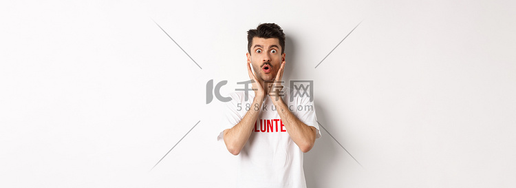 身穿志愿者 T 恤的震惊男子喘着粗气,敬畏地盯着镜头,站在白色背景上高清摄影大图 千库网