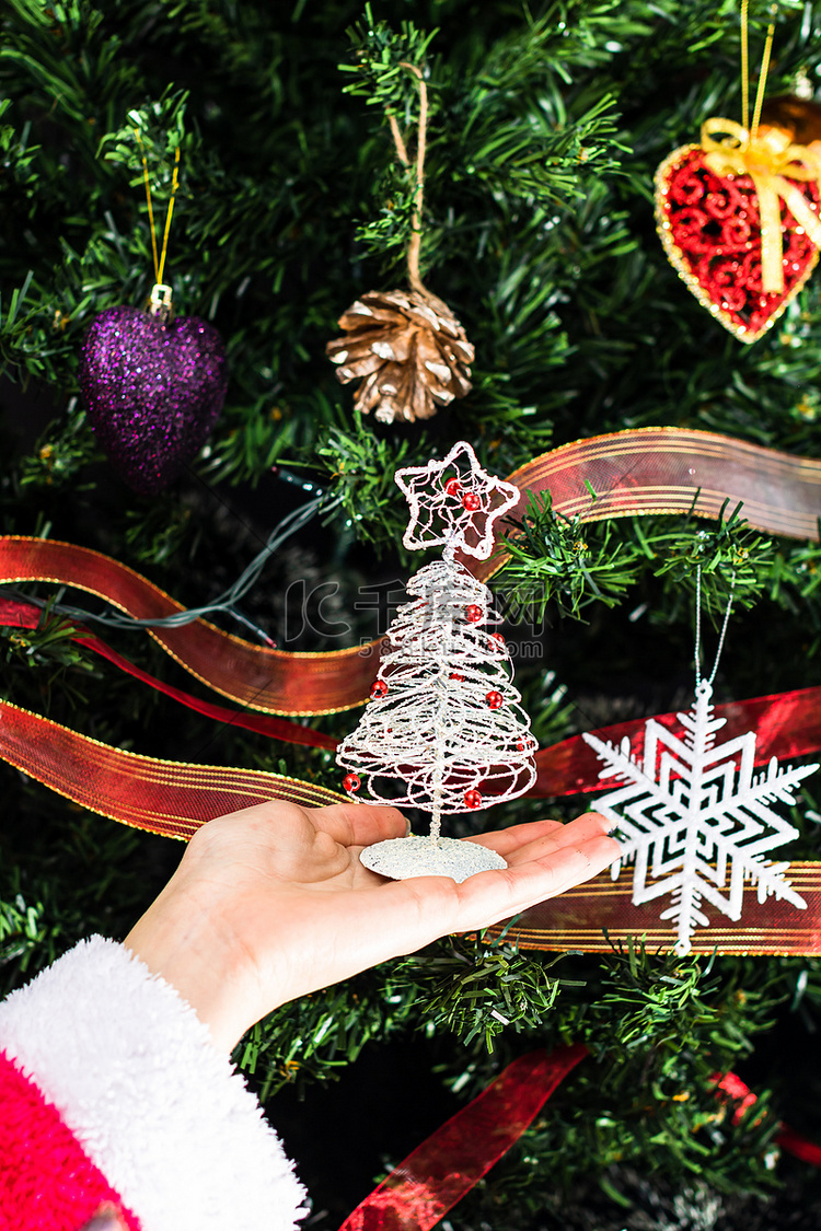 Hsnd 在圣诞树前拿着小圣诞树雕像。高清摄影大图-千库网