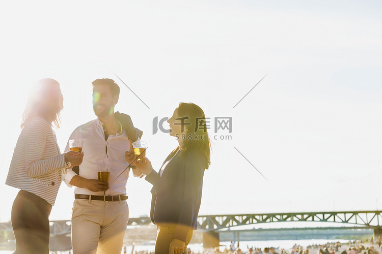 商人在海滩上喝啤酒庆祝成功，背景是镜头光晕高清摄影大图-千库网