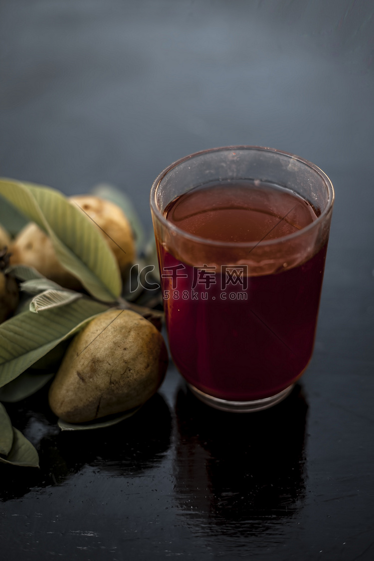 红番石榴或阿马鲁德或 jamrukh 有机汁的特写镜头，在透明玻璃杯中，木质表面上有生番石榴及其叶子。高清摄影大图-千库网