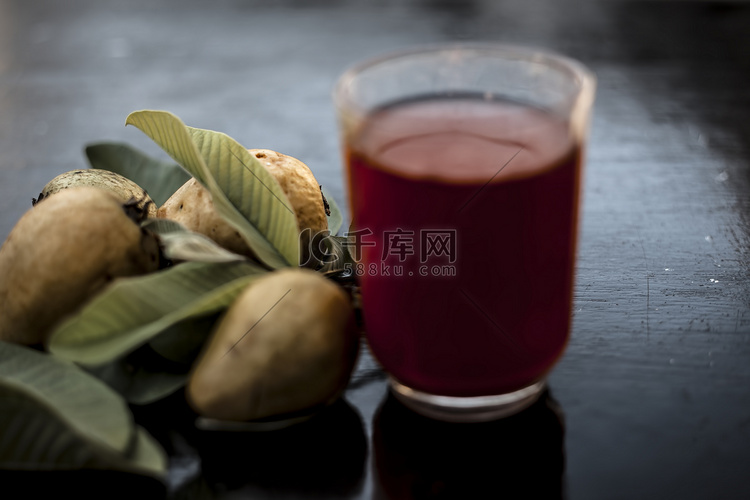 红番石榴或阿马鲁德或 jamrukh 有机汁的特写镜头，在透明玻璃杯中，木质表面上有生番石榴及其叶子。高清摄影大图-千库网