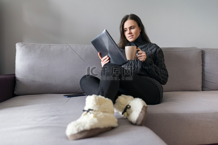 年轻女子坐在家里的沙发上，手里拿着小玩意高清摄影大图-千库网