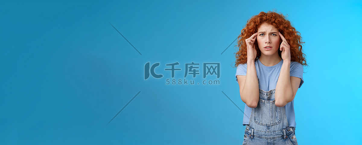 困惑惊慌的年轻苦恼的红发卷发女友皱着眉头触摸太阳穴无法集中注意力看起来困惑担心不记得尝试将情绪聚集在一起站在蓝色背景高清摄影大图-千库网