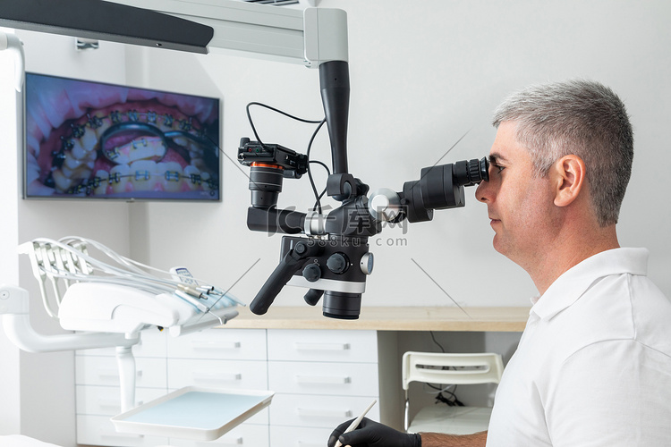 牙医在牙科诊所办公室使用牙科显微镜治疗患者牙齿。高清摄影大图-千库网