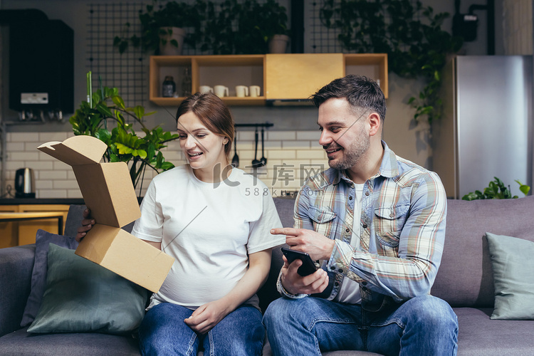 幸福的已婚夫妇在家丈夫和孕妇从网上商店收到包裹，高清摄影大图-千库网
