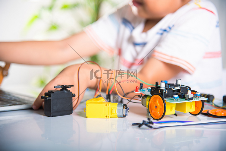亚洲男孩用笔记本电脑为 Arduino 机器人汽车学习编码和编程高清摄影大图-千库网