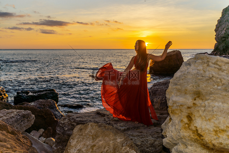 在夕阳的天空背景下，在海洋或海滩上穿着红色飞行礼服的舞蹈女子。高清摄影大图-千库网