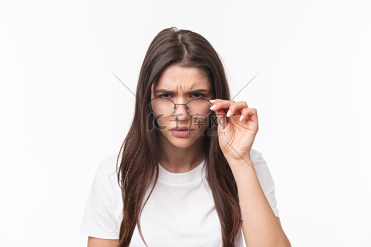 特写可疑的年轻严肃女性，从眼镜下看，眯着眼睛看着人，带着判断性的怀疑凝视，站在白色背景上，有疑问高清摄影大图-千库网