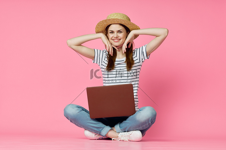 带笔记本电脑的快乐女人坐在粉红色背景的地板上高清摄影大图-千库网