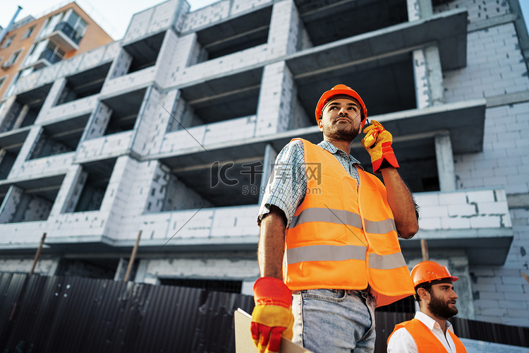 穿制服的年轻建筑工人在现场使用对讲机高清摄影大图-千库网