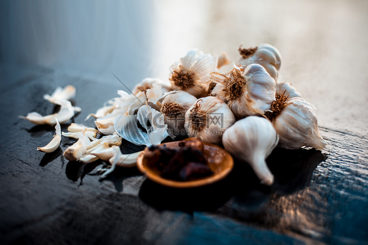 木制表面上的新鲜大蒜鳞茎或 lasun 以及小盘中的一些油炸大蒜丁香。用于治疗胆固醇。高清摄影大图-千库网