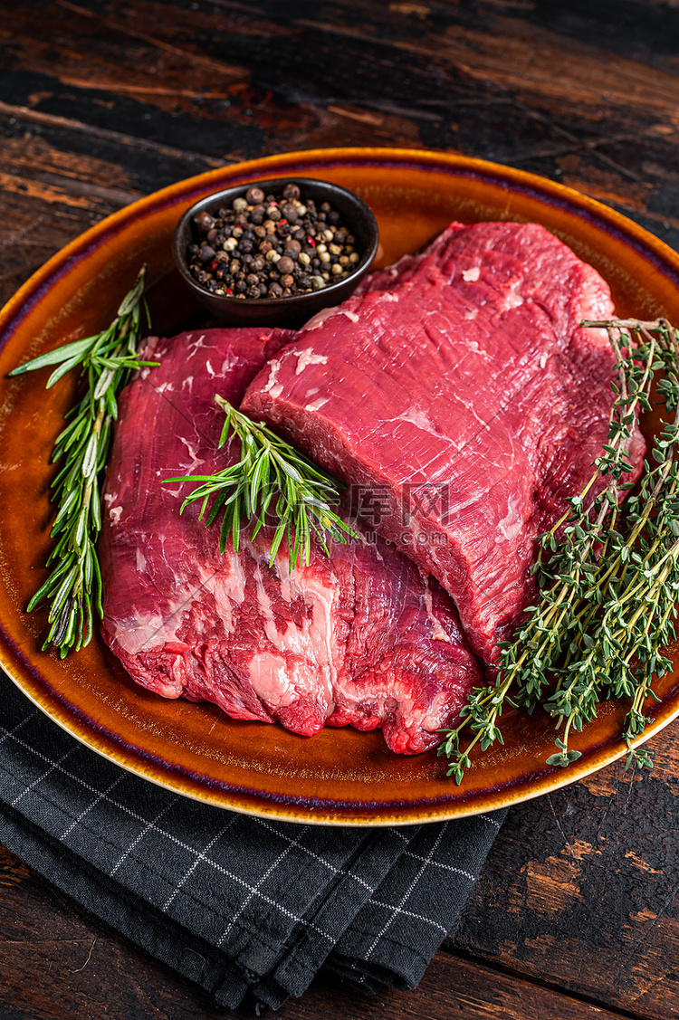 质朴的盘子上放着两块生牛肉牛排，上面放着香草。高清摄影大图-千库网
