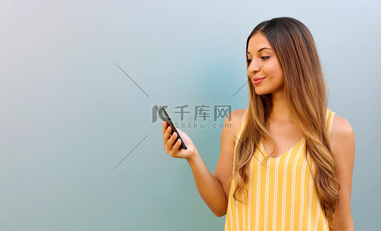 巴西女人在户外灰色背景下的智能手机上打字。高清摄影大图-千库网