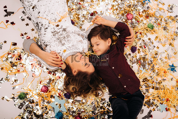 母亲和儿子躺在白色背景的五彩纸屑的地板上。高清摄影大图-千库网